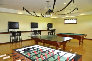 Quarto com mesa de futebol de mesa, mesa de sinuca e duas televisões fixadas na parede.