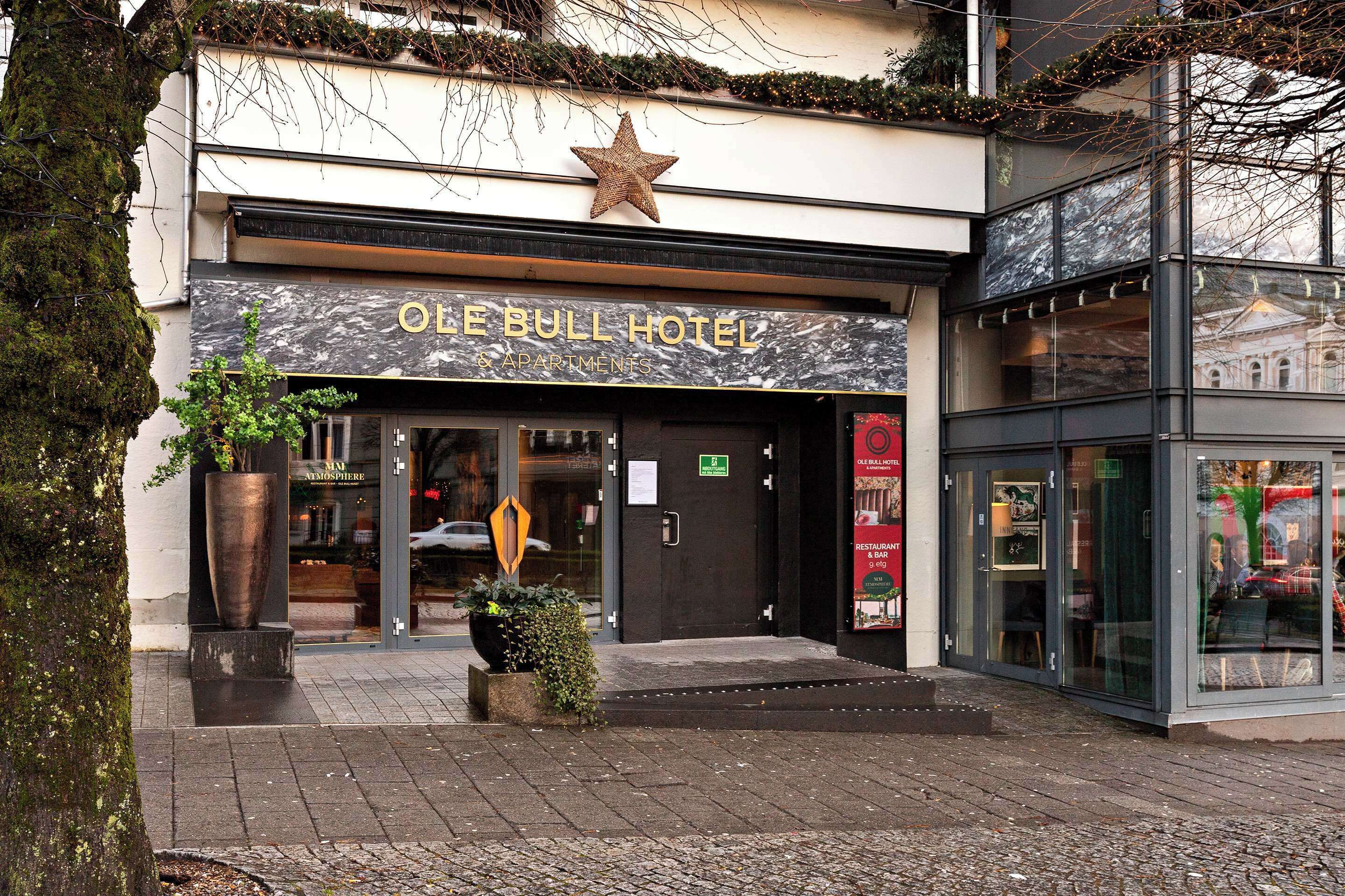 Exterior do Hotel Ole Bull, com uma estrela acima da entrada, um grande vaso de planta e fachada de vidro.