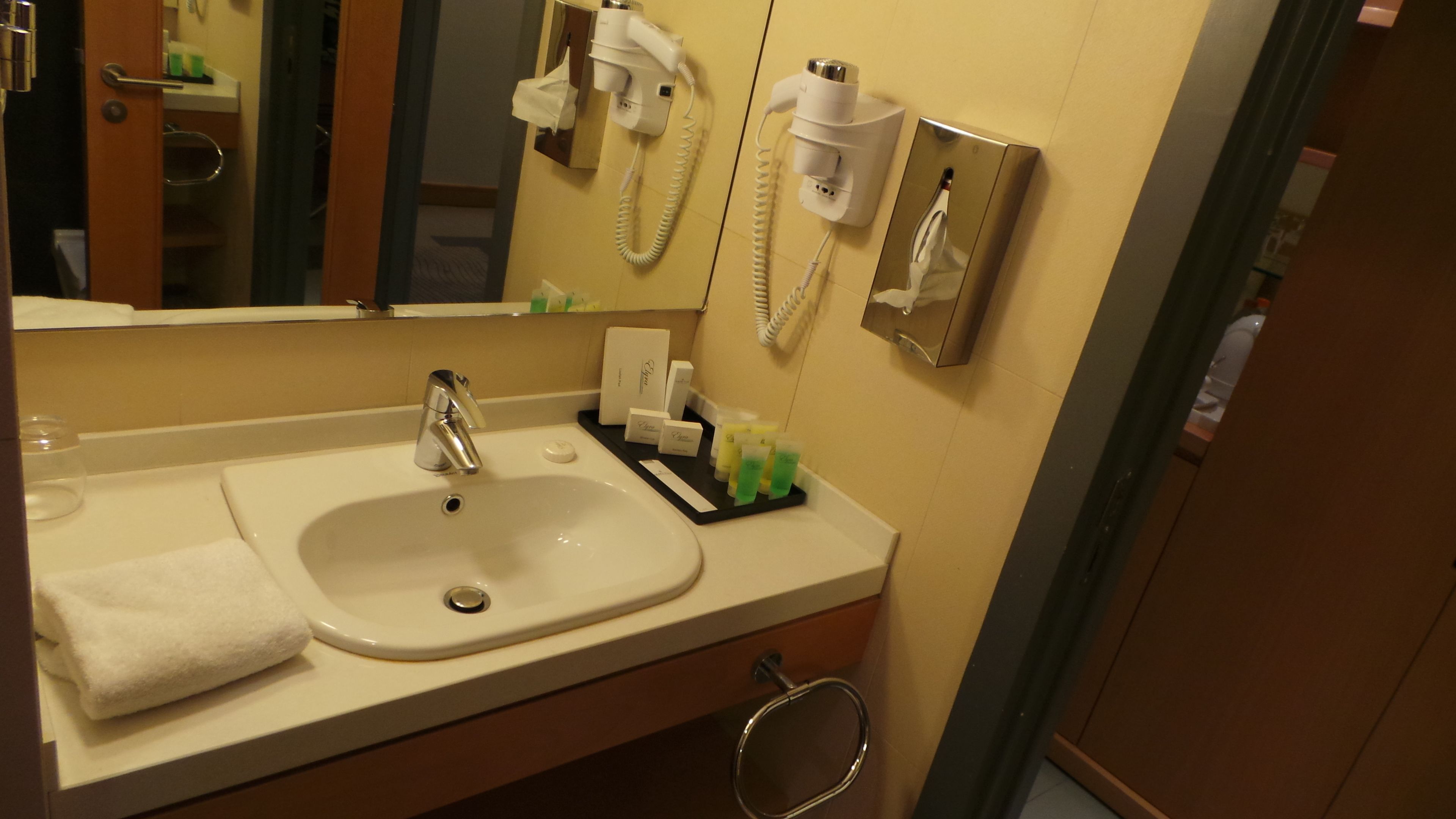 Casa de banho de hotel com lavatório, espelho, toalha, secador de cabelo e telefone.