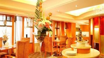 Um saguão de hotel com balcão de recepção central, área de estar com cadeiras e um arranjo de plantas decorativas.