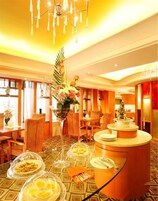 Um saguão de hotel com balcão de recepção central, área de estar com cadeiras e um arranjo de plantas decorativas.