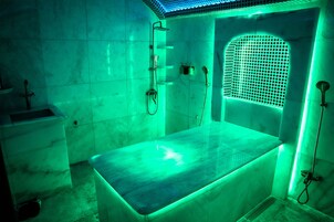 Um banheiro com pia de mármore, chuveiro com iluminação verde e parede revestida em azulejos.