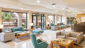 Um hall amplo com várias áreas de estar, um balcão de recepção e grandes janelas com vista para um jardim.