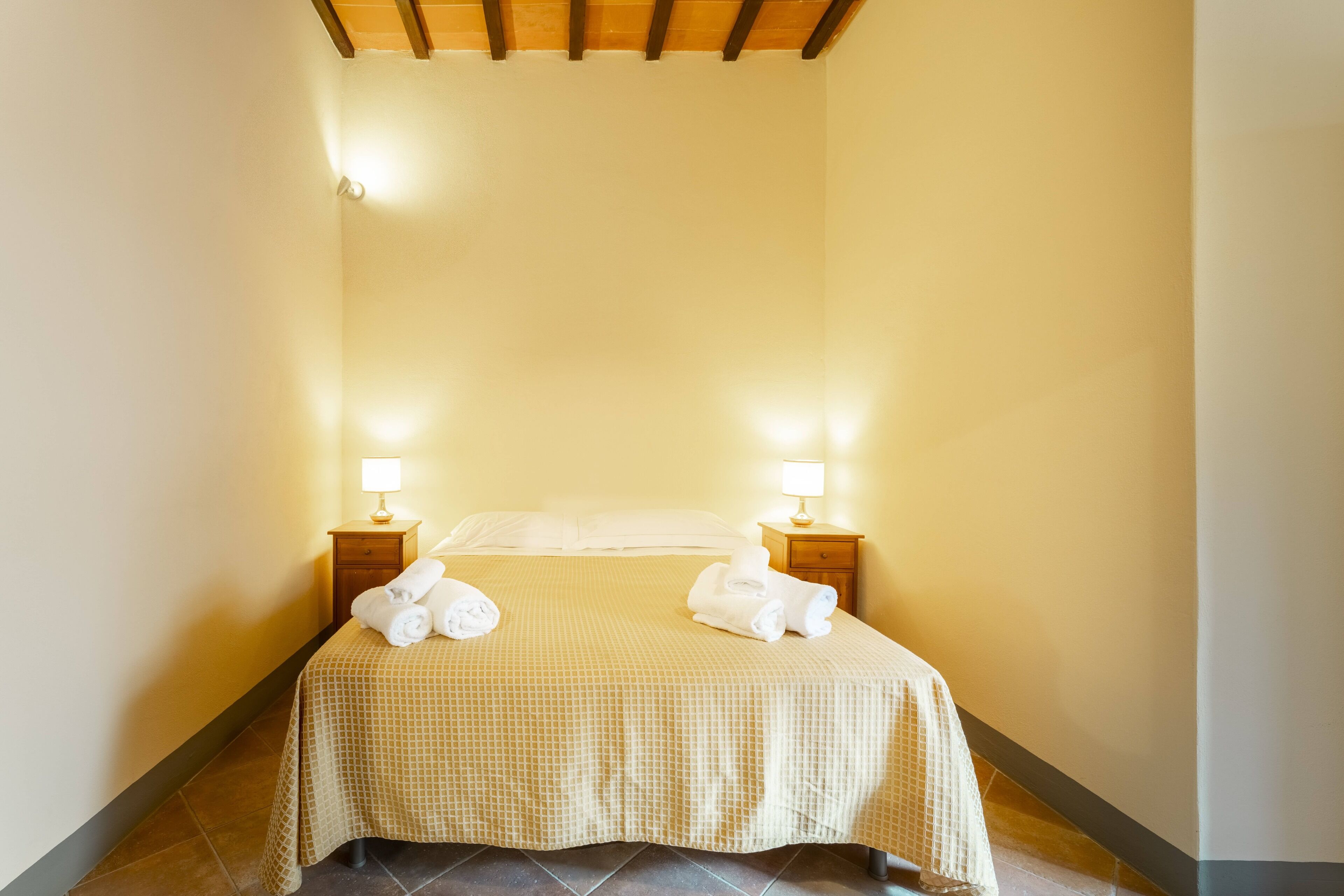 Quarto de hotel com cama, duas luminárias de cabeceira e duas toalhas sobre a cama.