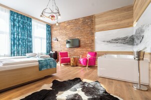 Quarto de hotel moderno com cama de madeira, uma janela grande com cortinas azuis, parede de tijolos, televisão montada, banheira branca e uma obra de arte pendurada.