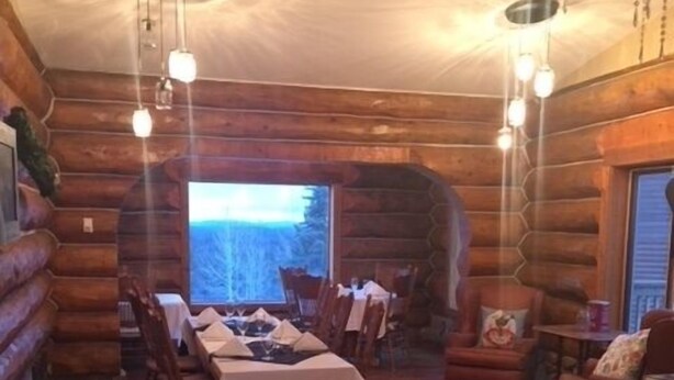 Interior de cabana de tronco com área de jantar, mesa posta para quatro pessoas e cadeiras de madeira ao redor.