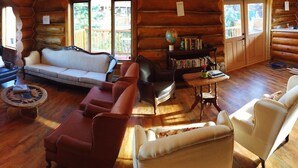 Interior acolhedor de uma cabana de madeira, com sofá, poltronas, mesa de centro e estante de livros.