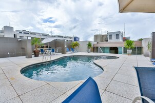 Piscina ao ar livre com espreguiçadeiras e uma palmeira.