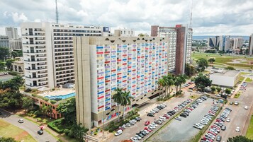 Um hotel de vários andares com design moderno, com um amplo estacionamento e um rio ao primeiro plano.