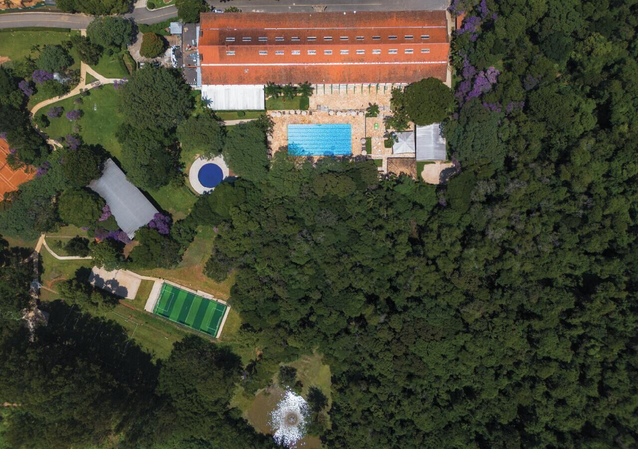 Vista aérea de uma propriedade com piscina, quadra de tênis e um edifício grande com telhado vermelho.
