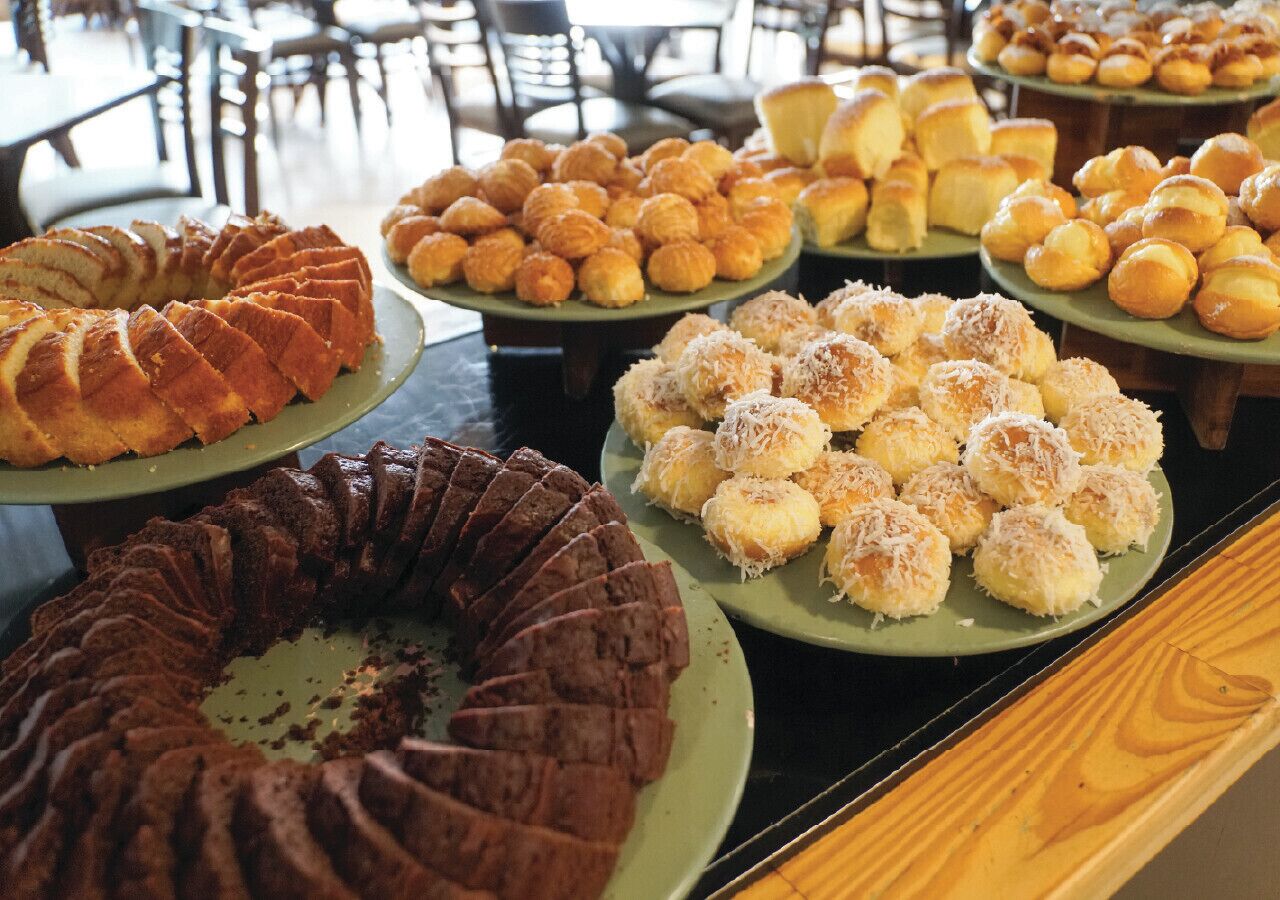 Diversos doces expostos, incluindo um bolo de chocolate, mini tortas de limão e doces cobertos de coco.