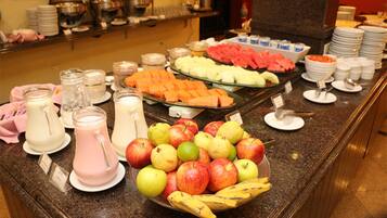 Buffet com diversas frutas, incluindo maçãs e bananas, e vários tipos de bebidas.