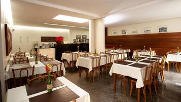 Um restaurante com várias mesas e cadeiras, uma área de balcão e quadros nas paredes.