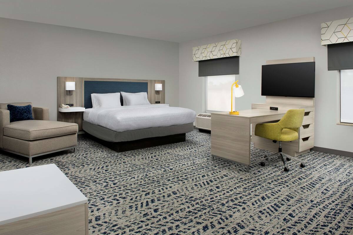 Quarto de hotel com cama, escrivaninha, cadeira, mesa de cabeceira e televisão de tela plana.