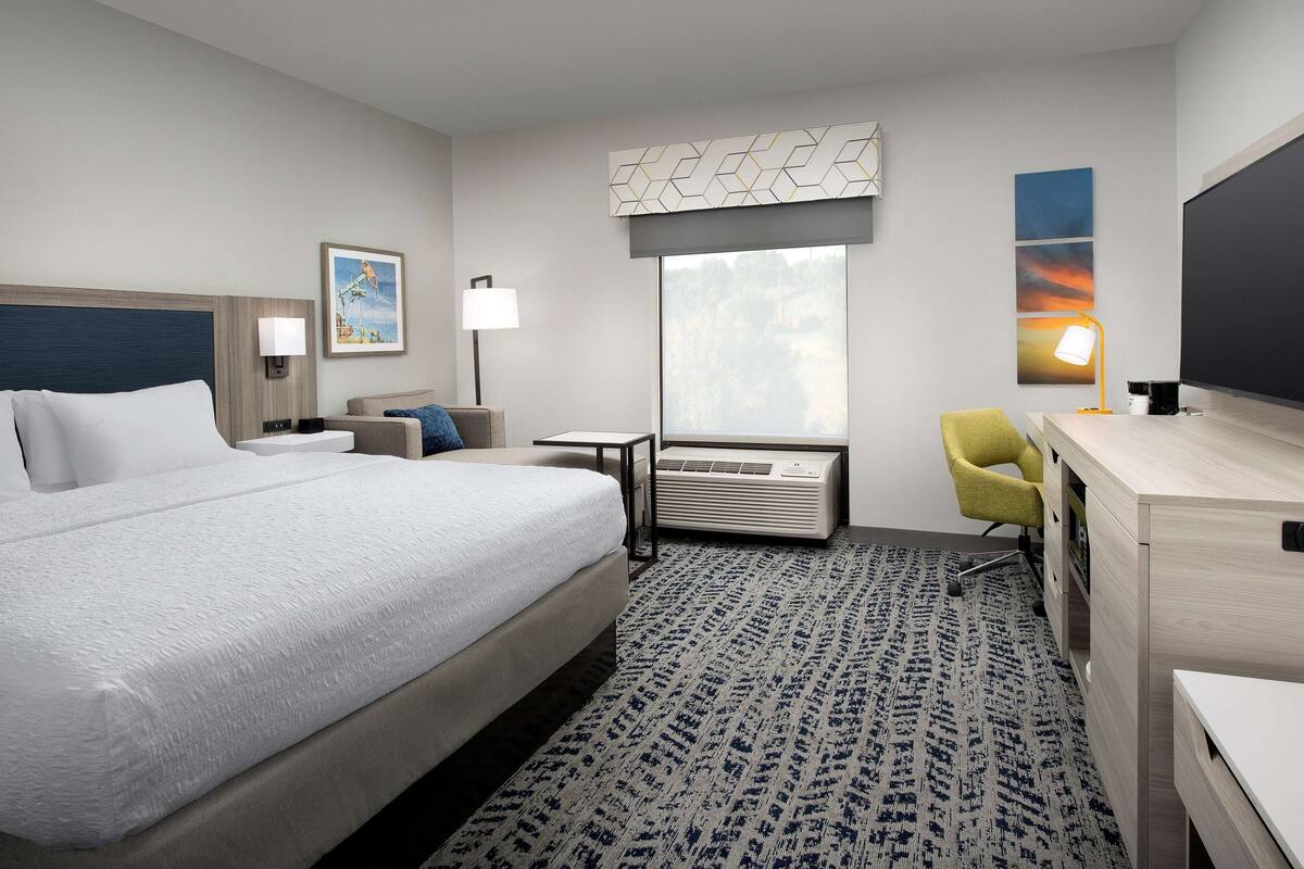 Quarto de hotel com uma cama grande, uma escrivaninha, uma cadeira, uma televisão, uma janela com vista e um ar-condicionado fixado na parede.
