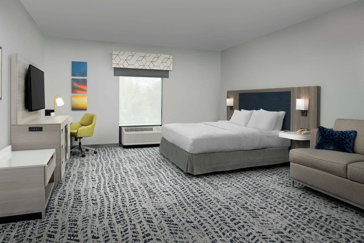 Quarto de hotel com cama, escrivaninha, cadeira, televisão e janela.