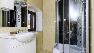 Casa de banho com toucador branco, cabine de duche com vidro e espelho sobre a pia.