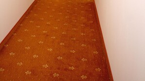 Um corredor longo e estreito, com portas em ambos os lados, piso coberto de carpete e obras de arte nas paredes.