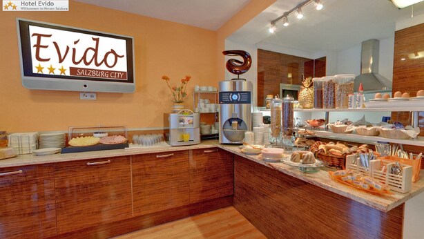 Espaço de café da manhã de hotel com buffet, incluindo diversos alimentos e uma máquina de café.