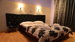 Cama bem arrumada com colcha floral, cabeceira preta e duas luzes fixadas na parede.