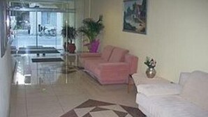 Um saguão de hotel com um balcão de recepção, um sofá rosa, um sofá branco e um tapete estampado.