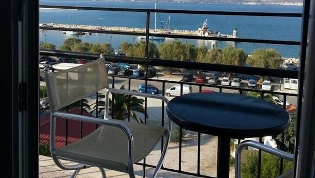 Varanda com duas cadeiras e uma mesa pequena, com vista para uma marina e uma paisagem montanhosa.