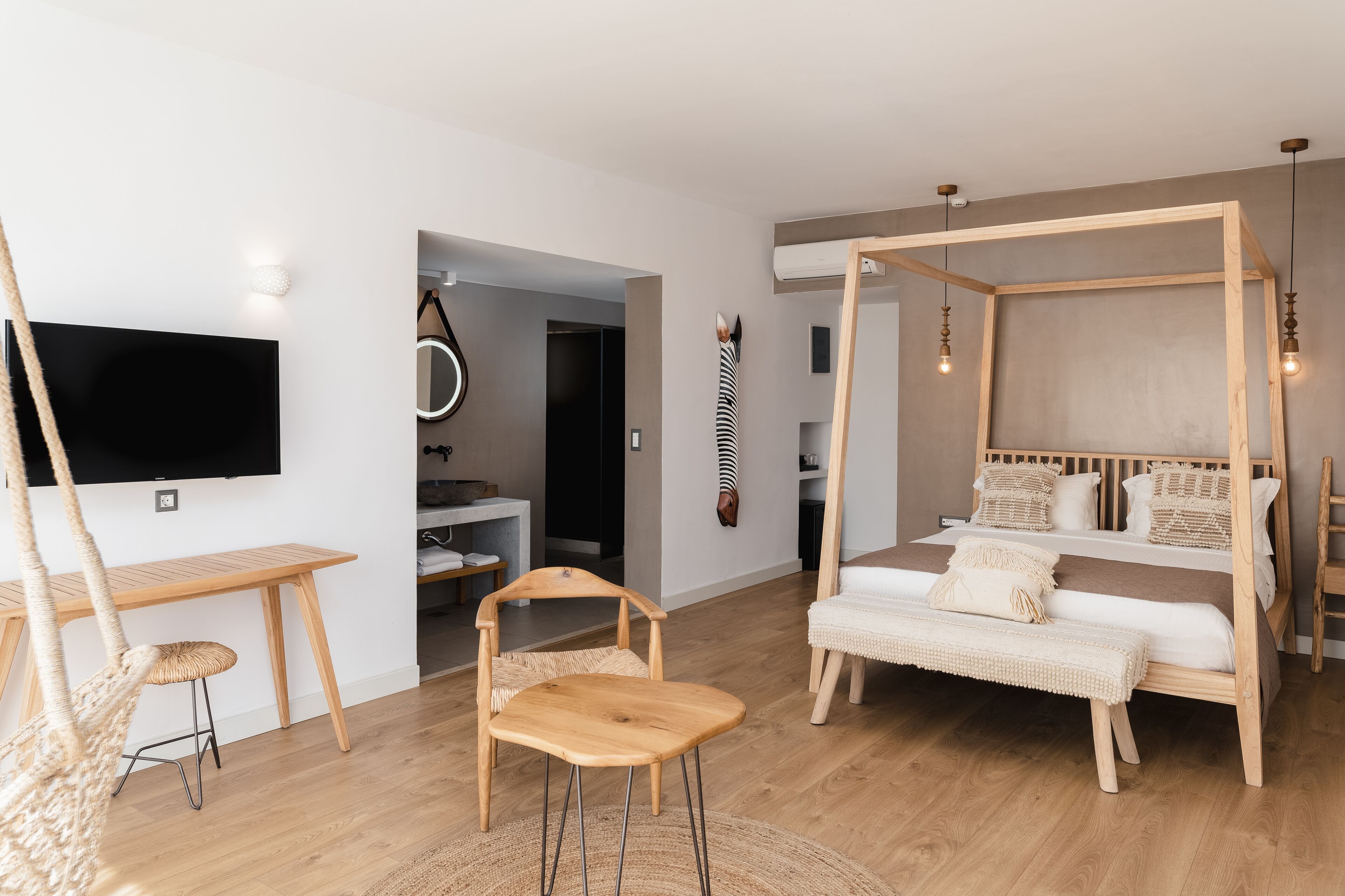 Quarto moderno com uma cama de dossel de madeira, uma escrivaninha com cadeira, uma TV fixada na parede e um banquinho pequeno.