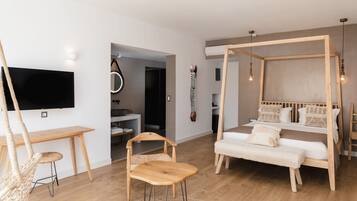 Quarto moderno com uma cama de dossel de madeira, uma escrivaninha com cadeira, uma TV fixada na parede e um banquinho pequeno.