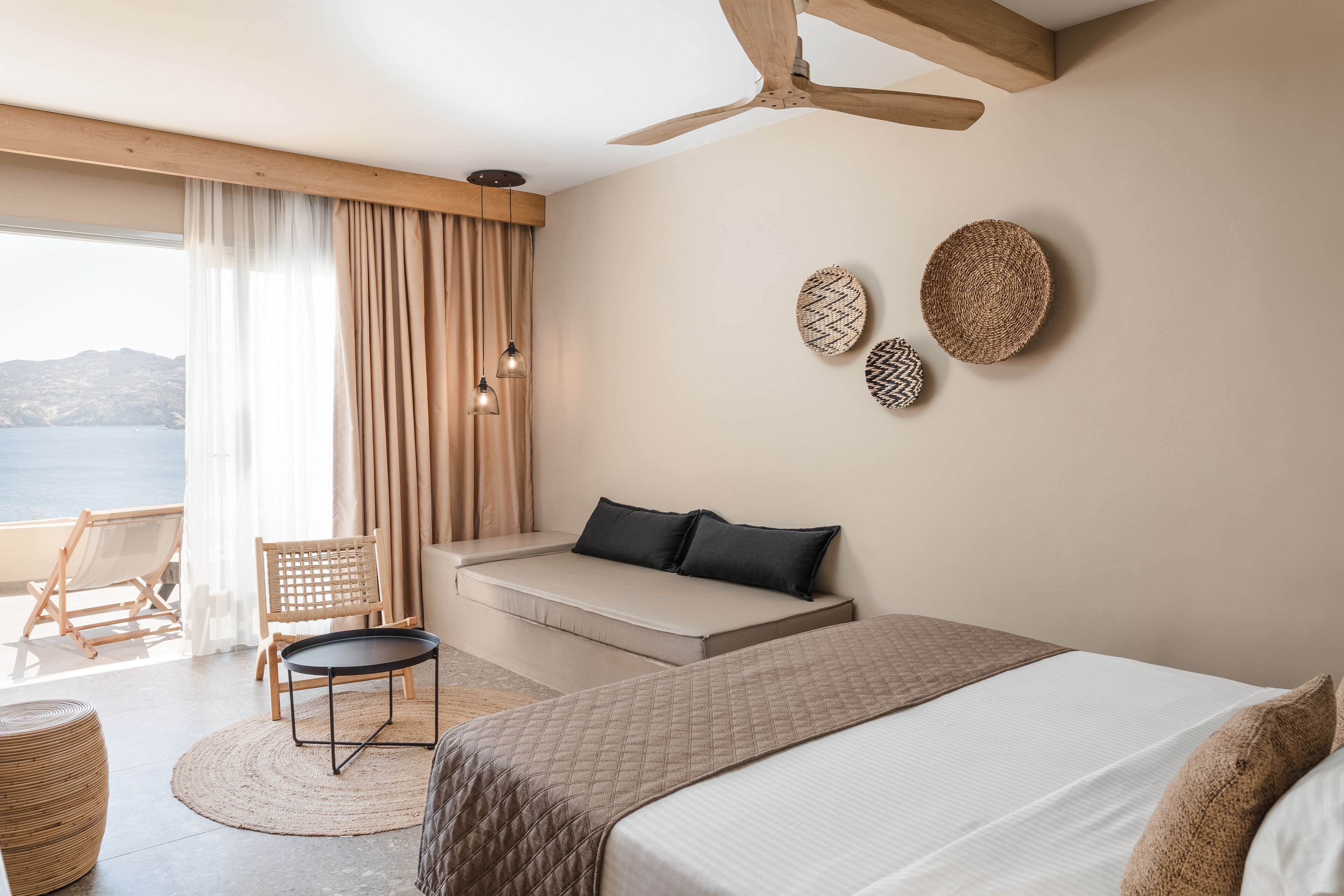 Quarto com cama, sofá, cadeira, mesa redonda e vista para o mar.