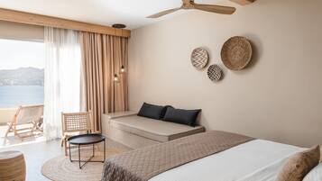 Quarto com cama, sofá, cadeira, mesa redonda e vista para o mar.