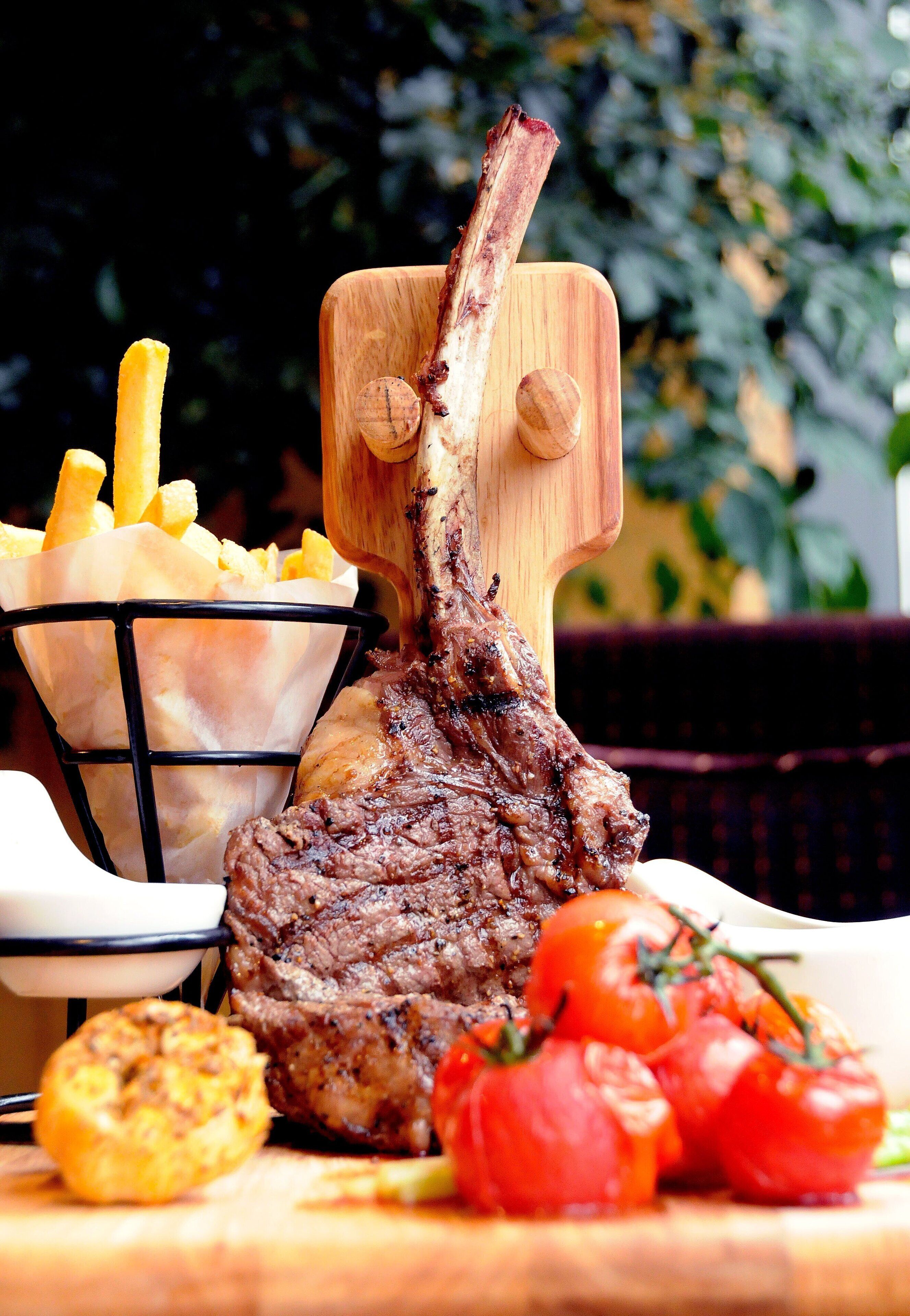 Paleta de cordeiro sobre tábua de madeira, com cesta de batatas fritas e tomate cereja.