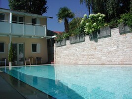 Uma piscina com água cristalina, uma parede de pedra e um edifício com varanda.