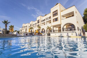 Um hotel com várias varandas, piscina e palmeiras.