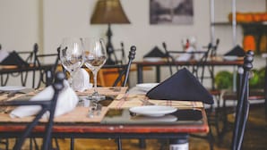 Mesa de jantar posta com taças de vinho, pratos e talheres, com um abajur e um quadro emoldurado ao fundo.