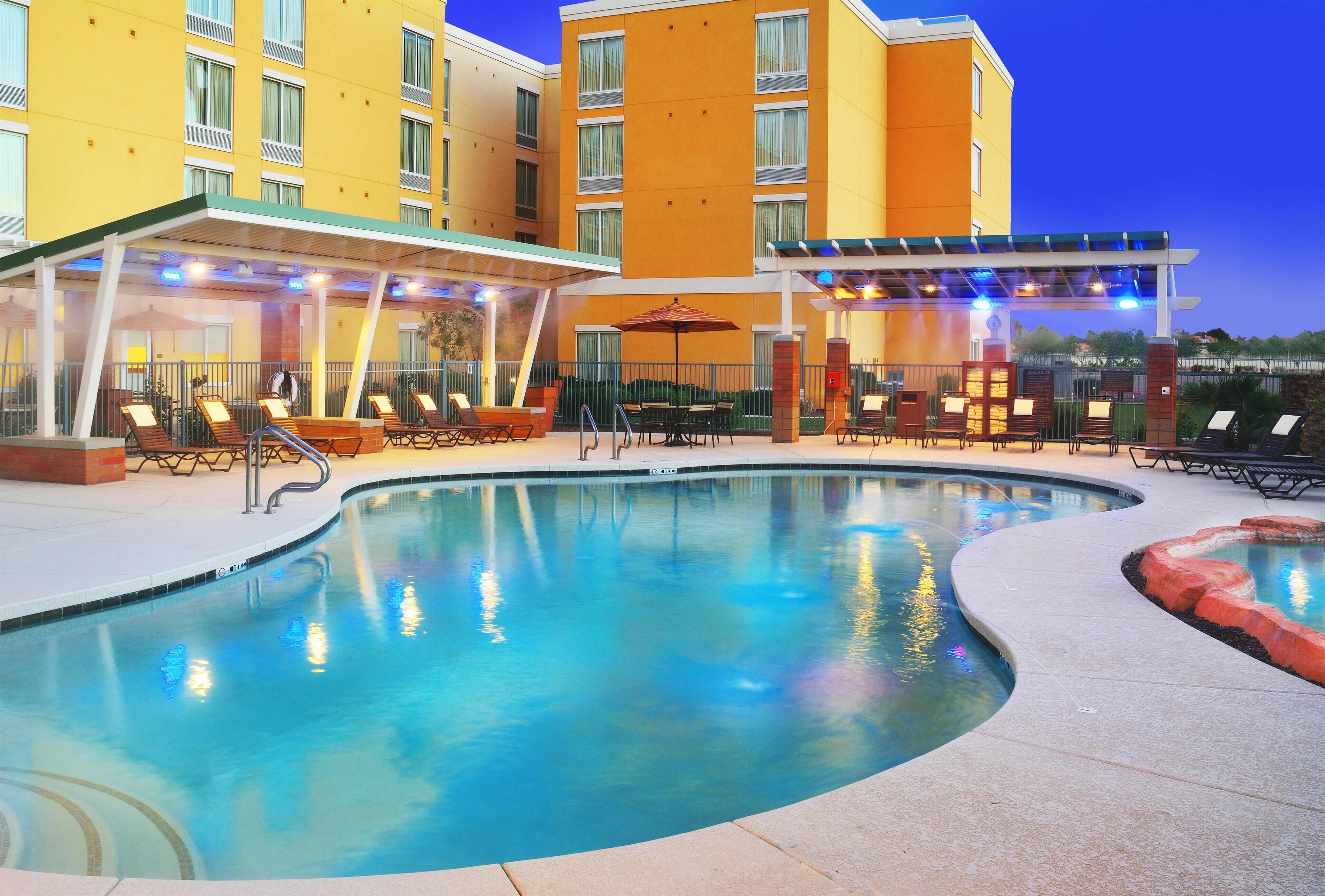 Uma área de piscina de hotel com espreguiçadeiras e guarda-sóis, rodeada por um edifício com vários andares e varandas.