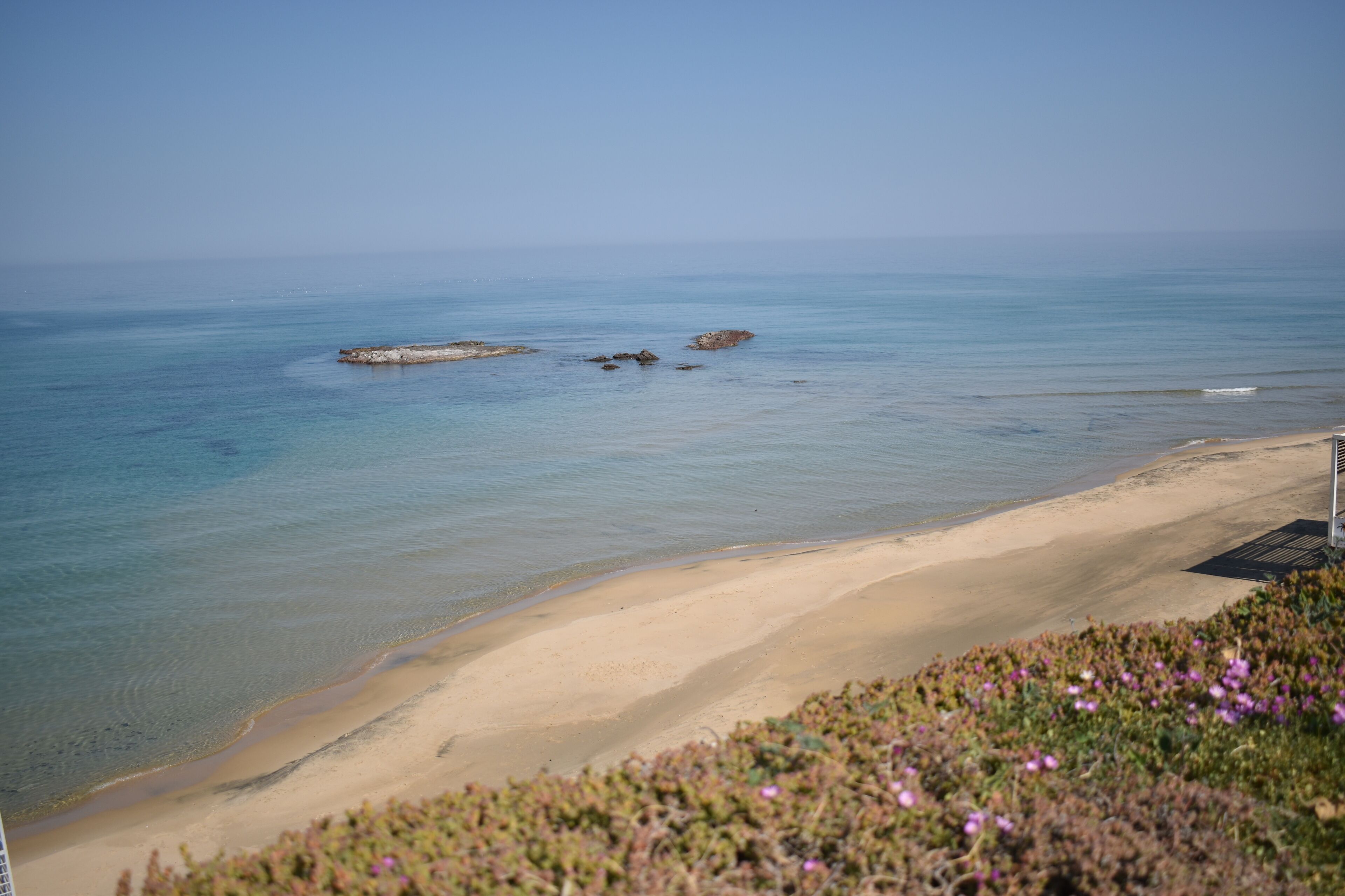 Uma praia com águas cristalinas, areal arenoso e algumas rochas.