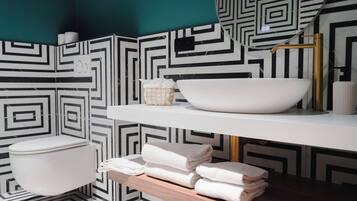 Um banheiro moderno com padrão geométrico de azulejos preto e branco, uma pia branca com torneira dourada e um vaso sanitário.