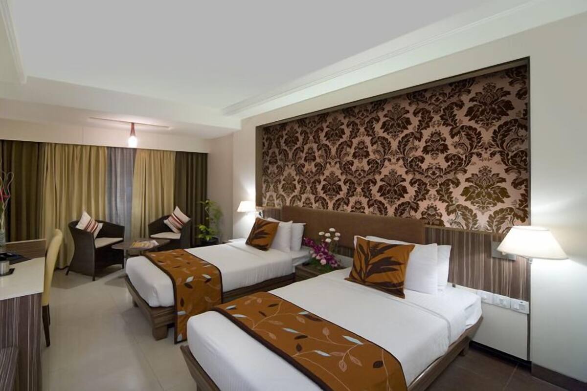 Quarto de hotel com duas camas, uma escrivaninha, uma cadeira, uma televisão e um papel de parede estampado.