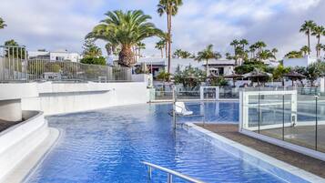 Piscina com barreira de vidro, palmeiras e edifícios modernos ao fundo.