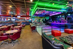 Uma área de bar com mesas e cadeiras, um palco com equipamentos musicais e um balcão.