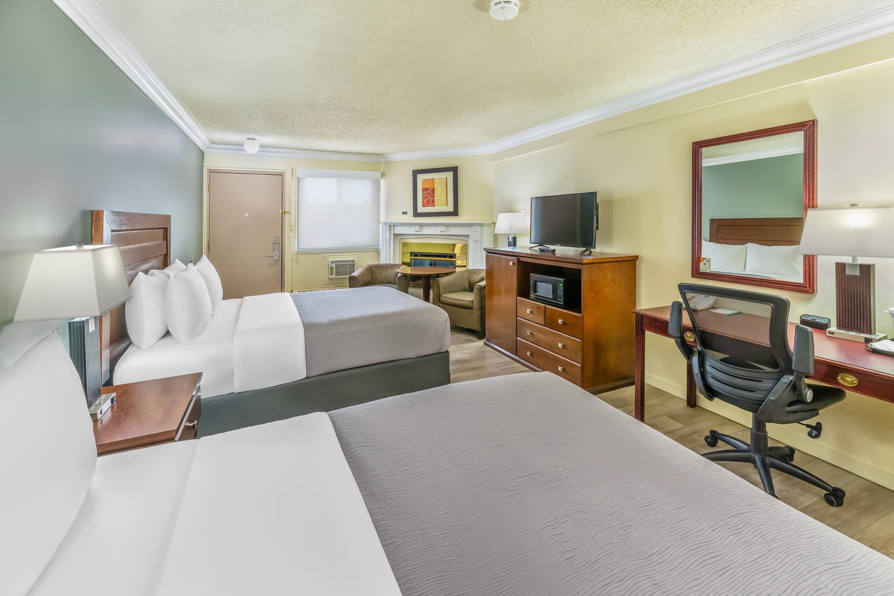 Quarto de hotel com duas camas, uma escrivaninha, uma cadeira, televisão e lareira.