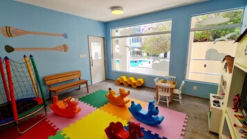 Uma sala de jogos infantil com um banco, tapetes de atividades coloridos e brinquedos.