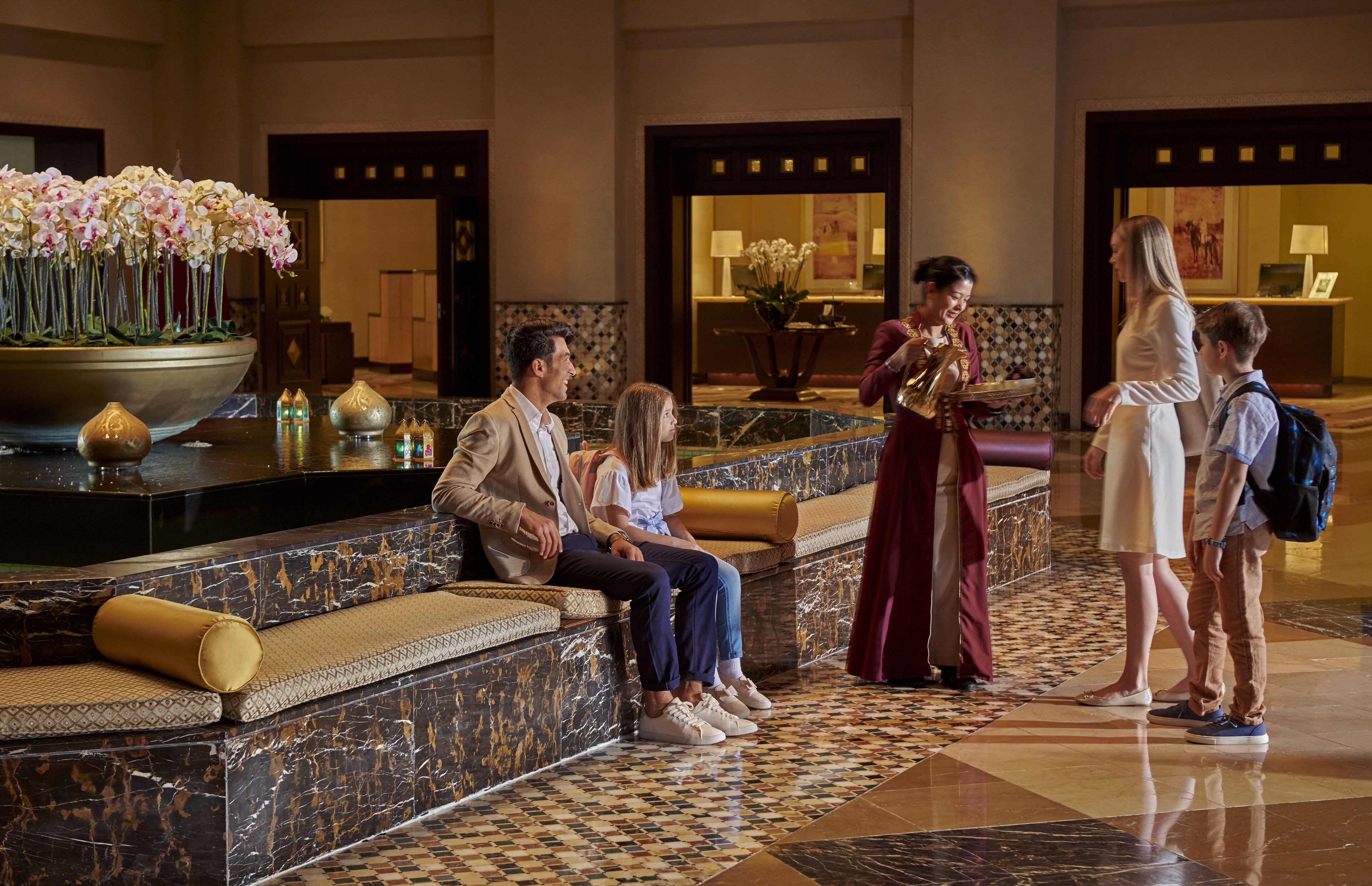 Um lobby com uma recepção de mármore, um vaso grande de flores e uma área de estar com almofadas.