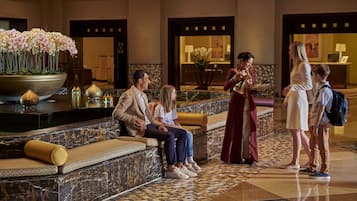 Um lobby com uma recepção de mármore, um vaso grande de flores e uma área de estar com almofadas.