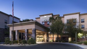 Entrada de hotel com galeria coberta, palmeiras e placa da Homewood Suites by Hilton.
