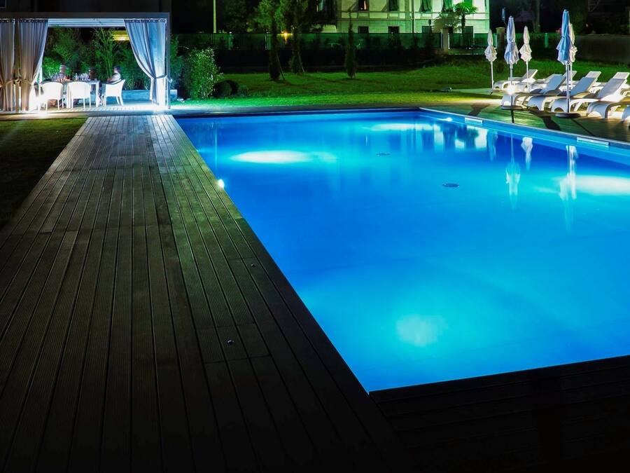 Piscina com deck de madeira, cadeiras de espreguiçadeira e guarda-sóis.