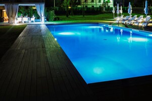 Piscina com deck de madeira, cadeiras de espreguiçadeira e guarda-sóis.