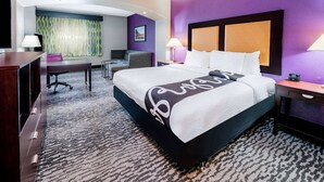 Quarto de hotel com uma cama grande, uma escrivaninha, uma cadeira e uma televisão.