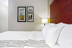 Quarto de hotel com cama bem arrumada, mesa de cabeceira com abajur e três quadros na parede.