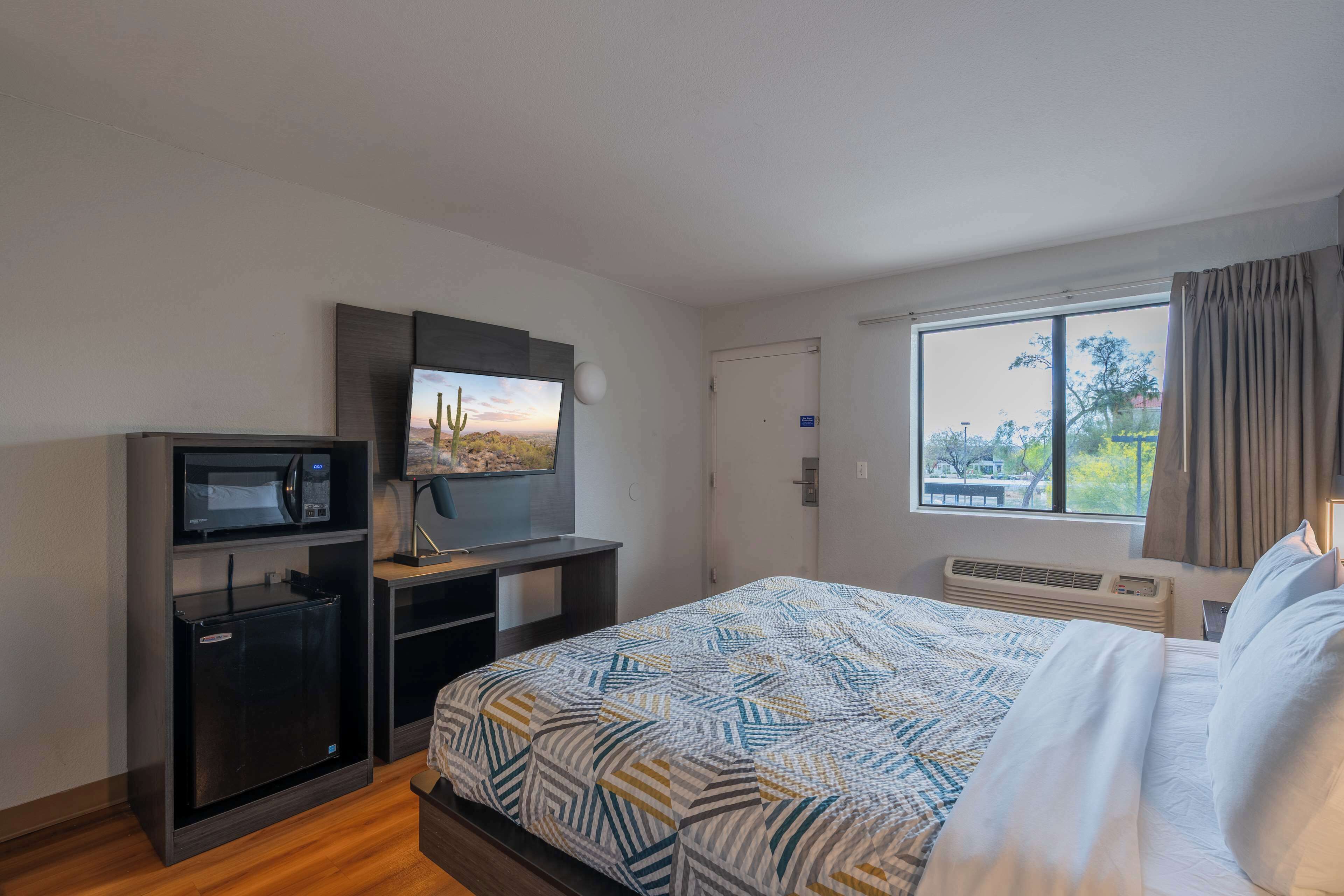 Quarto de hotel com cama, televisão, micro-ondas e frigorífico pequeno.